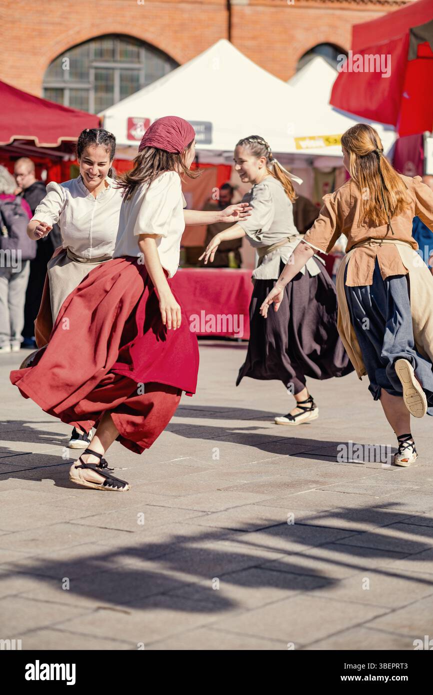 Four young women in medieval costumes are dancing in a public square ...
