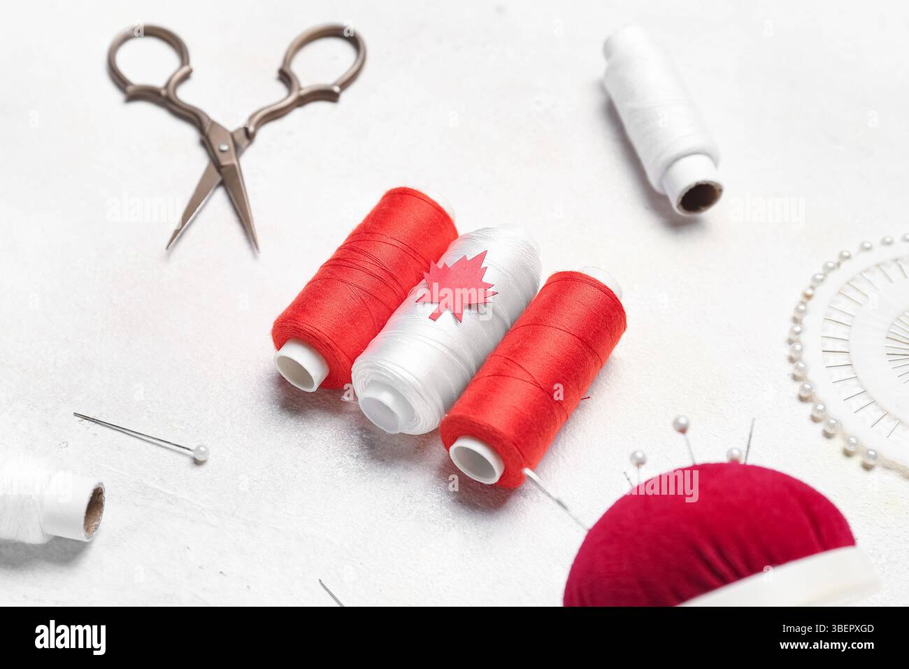 Thread spools with maple leaf, pin cushion and scissors on white ...