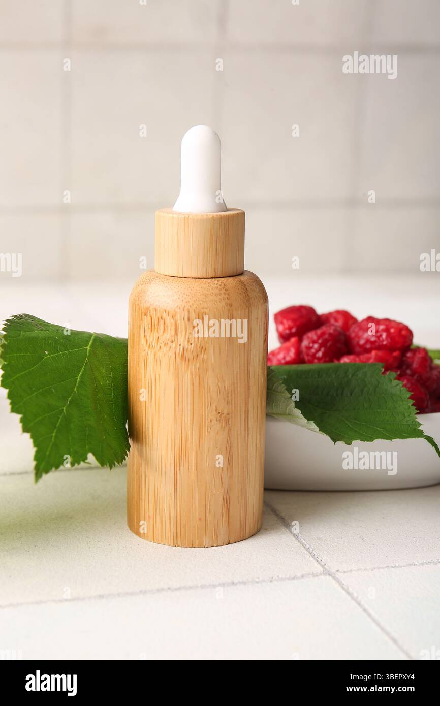 Bottle of cosmetic raspberry oil and bowl with berries on white tile ...