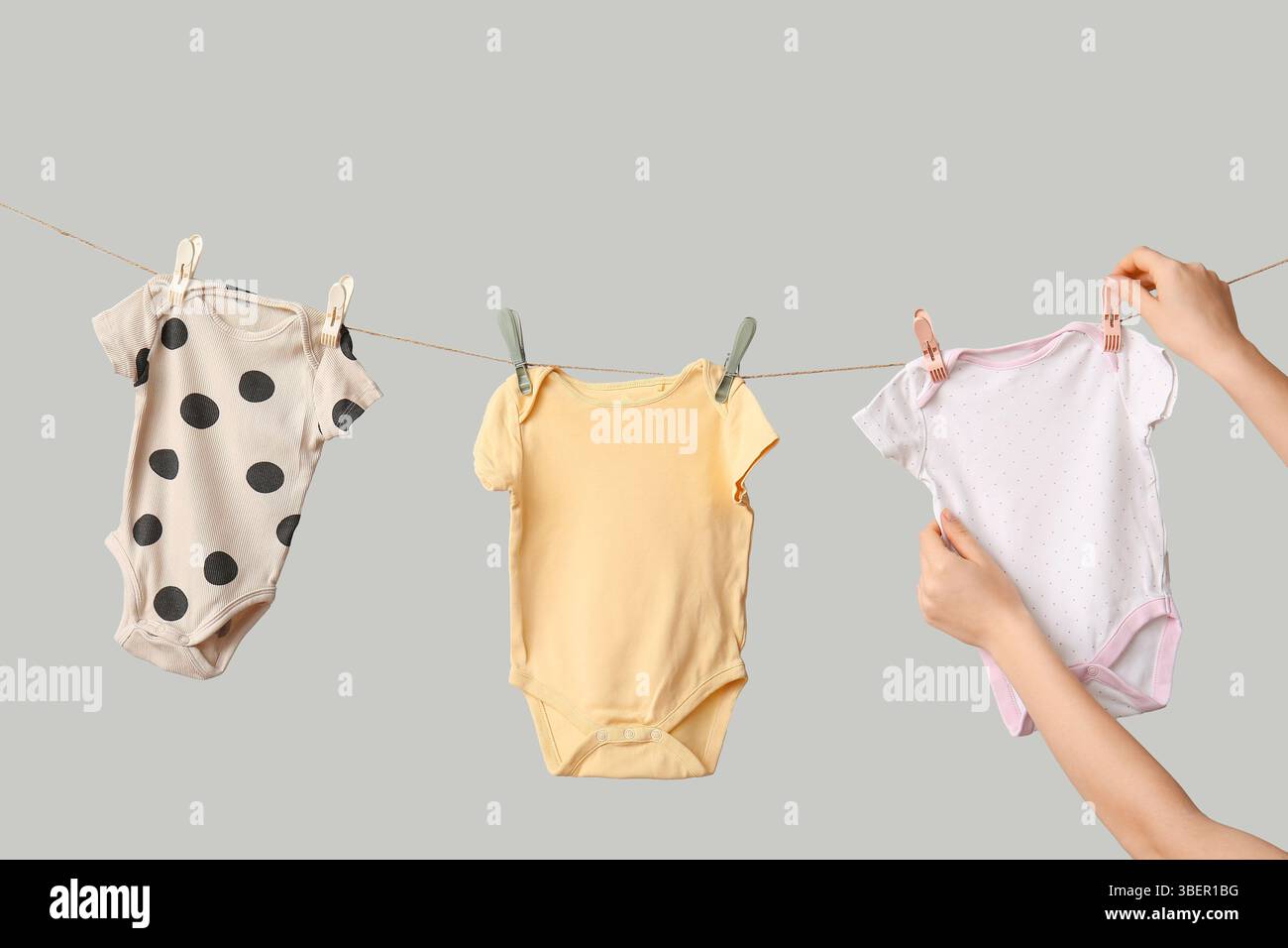 Hands and baby clothes hanging on clothesline against grey background ...