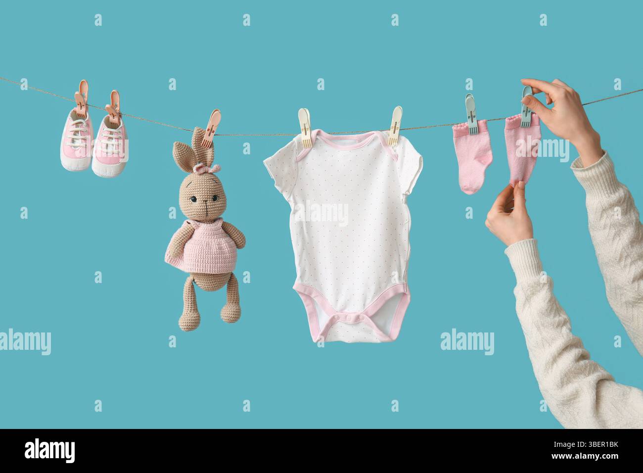Hands with baby clothes and toy hanging on clothesline against blue ...