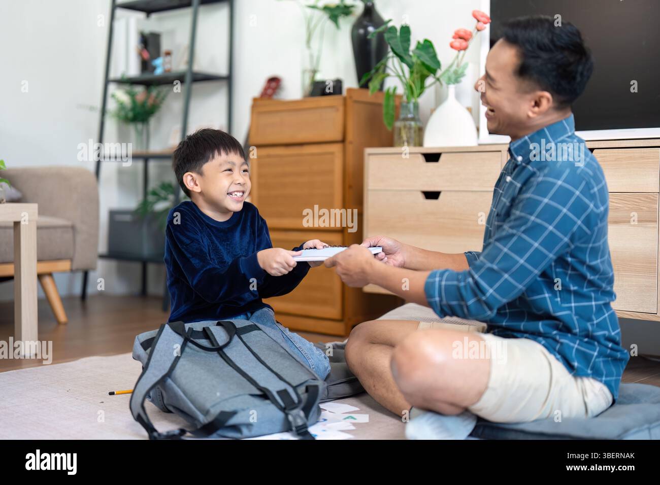 Father and son sharing a joyful moment while packing school supplies ...