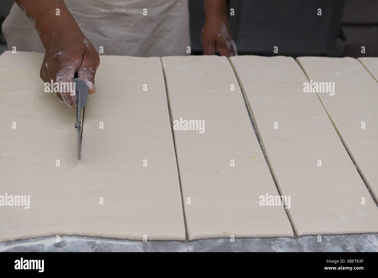 A baker's hands expertly slice a sheet of dough into even strips using ...