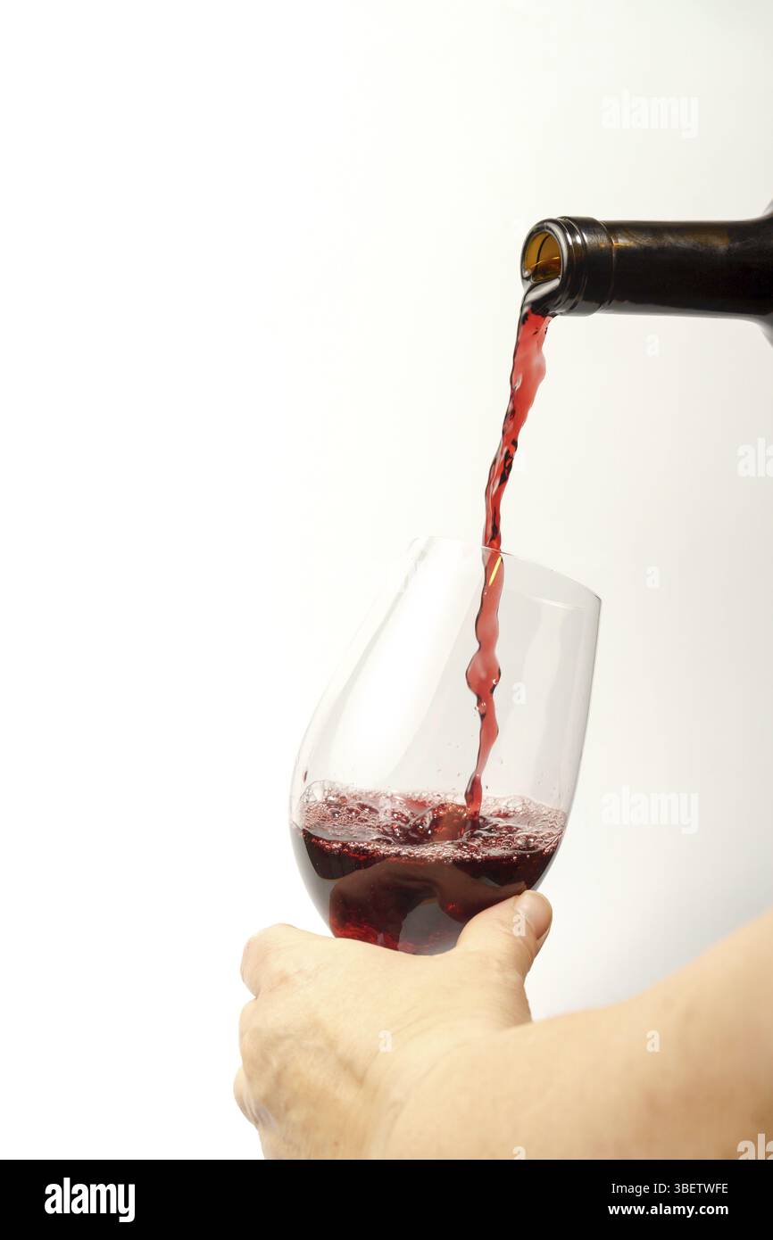 Hand pouring red wine from bottle into glass on plain white background ...