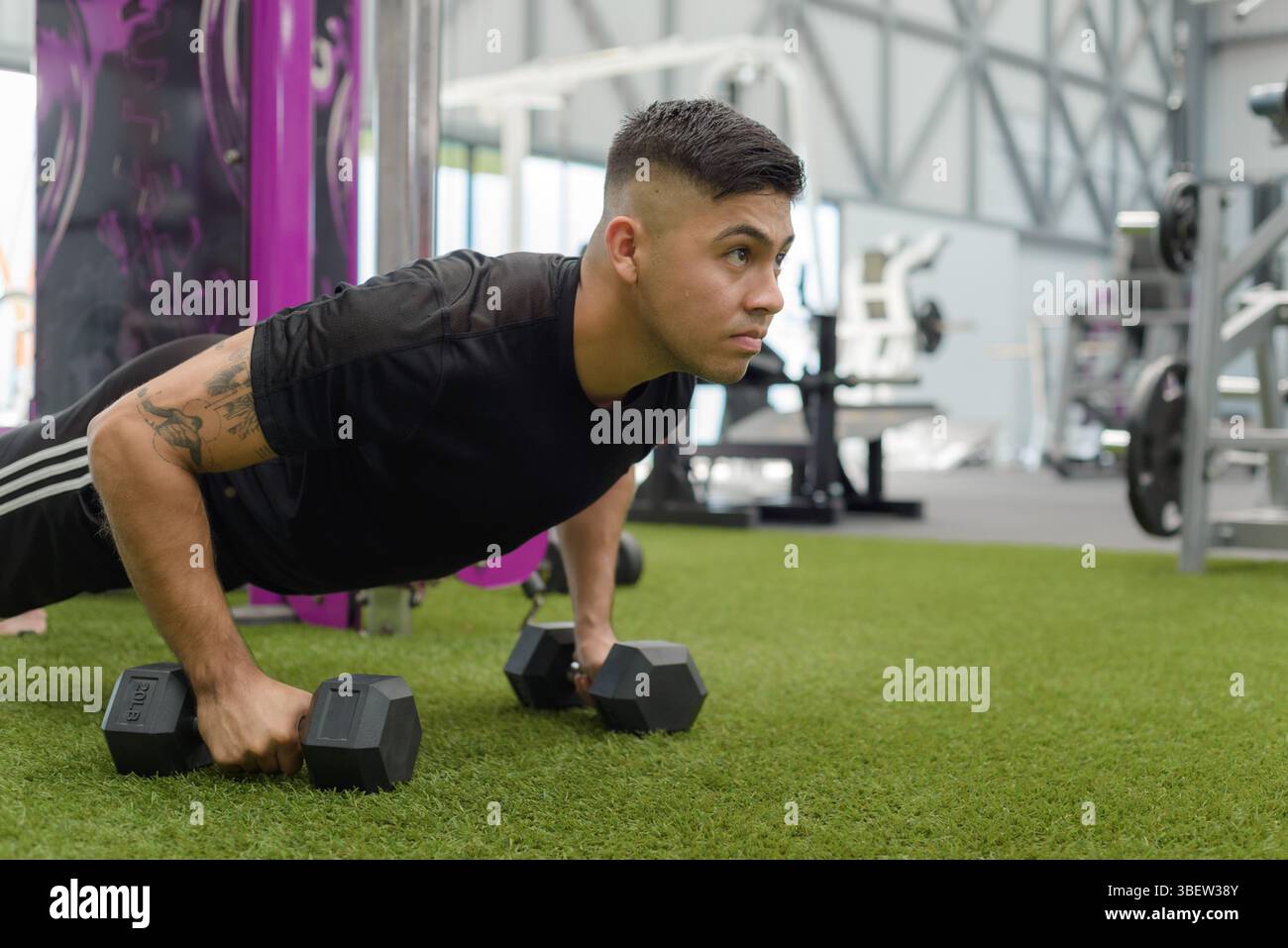 A determined man performs dumbbell push-ups on artificial turf in a ...