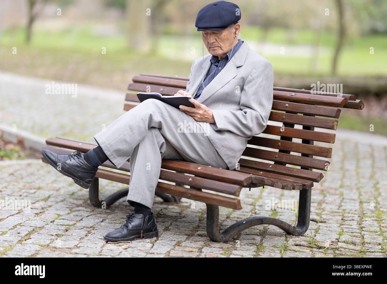 Elderly writer taking notes in notebook while sitting on park bench ...
