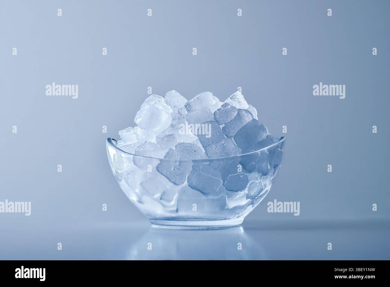 Glass bowl with a pile of ice cubes backlit on a reflective base with ...