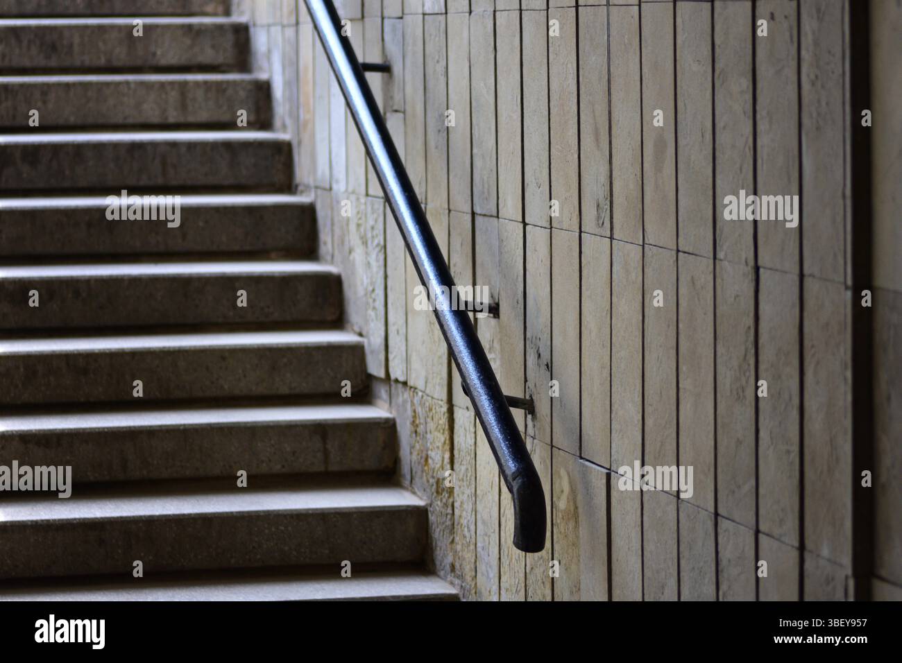 Close-up view of a black metal handrail on a tiled wall beside concrete ...