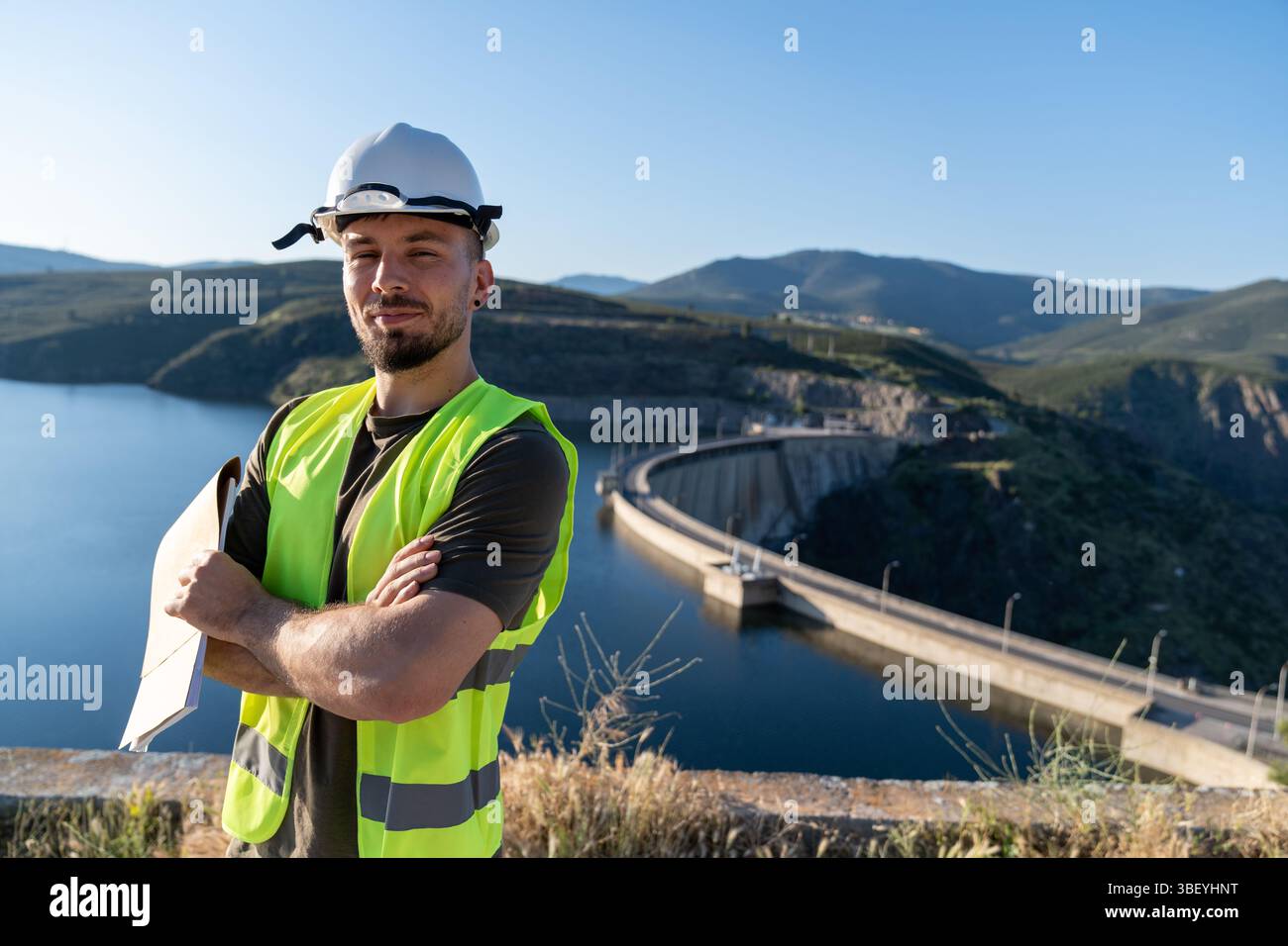 Engineer holding blueprints supervising construction of hydroelectric ...