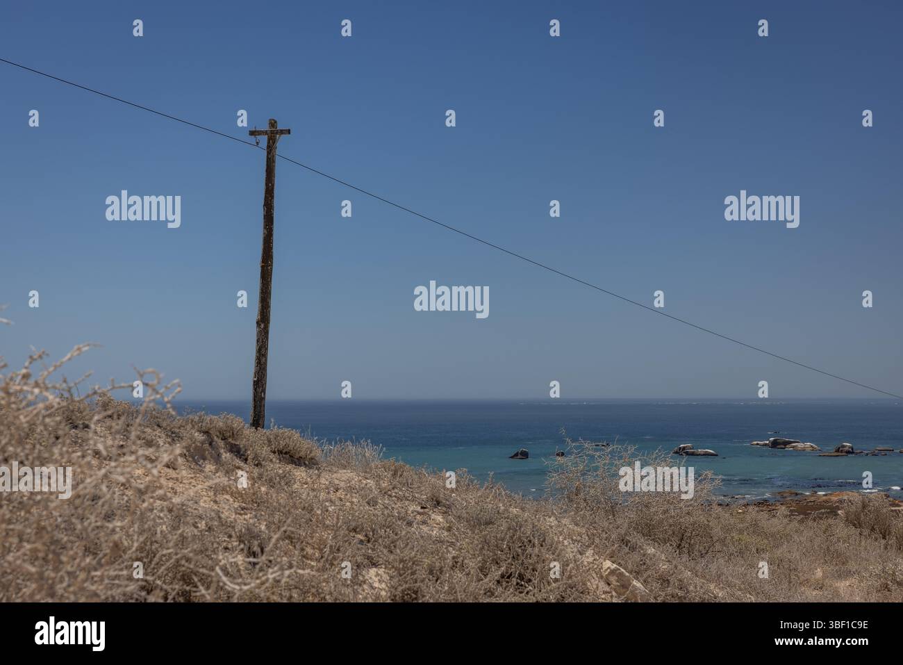Single wooden utility pole with taut wire seen on a dry coastal slope ...
