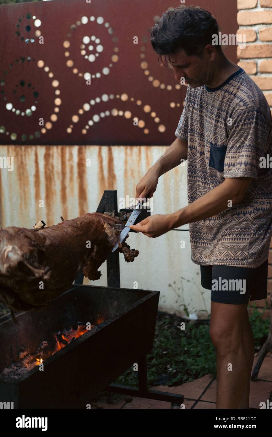 Man carving spit-roast meat over open fire Stock Photo - Alamy