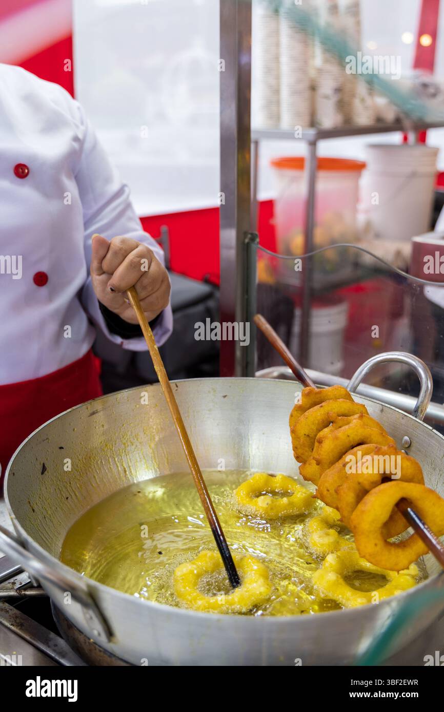 A woman is cooking picarones in a pan. The food is being cooked on a ...