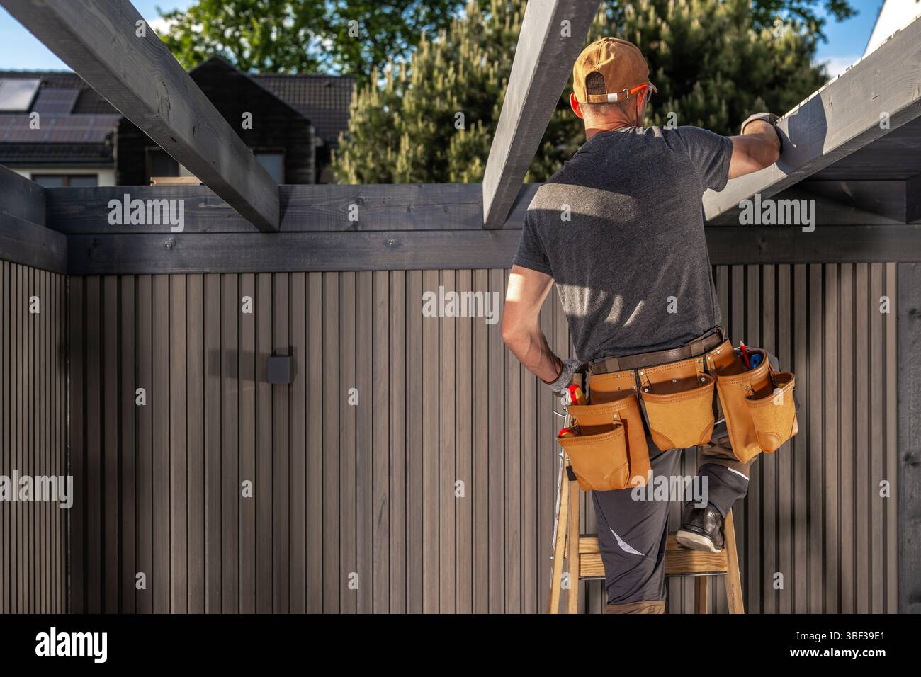 A construction worker stands on a ladder, focusing on repairing wooden ...