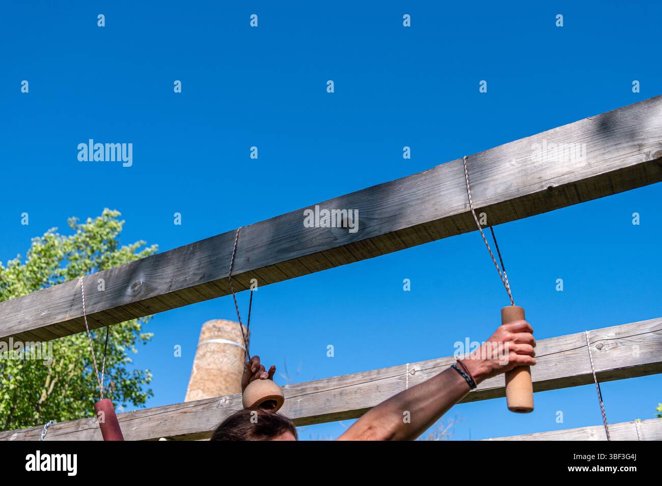 athletic man doing a pull up exercise on an outdoor wooden obstacle ...
