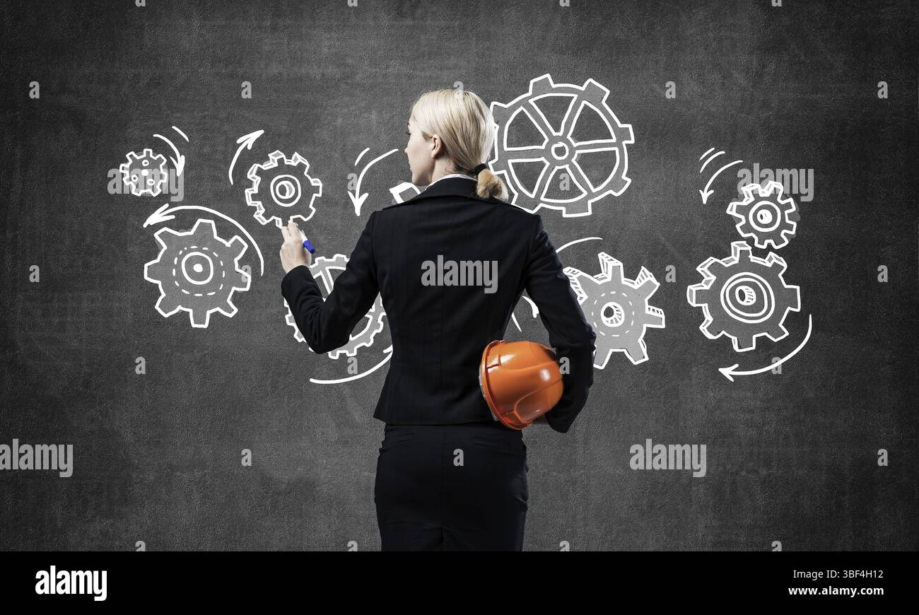 Businesswoman draws cogwheel mechanism on chalkboard. Woman in business ...