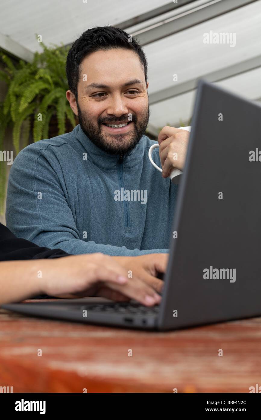 Man in blue works on laptop as colleague writes beside him, symbolizing ...