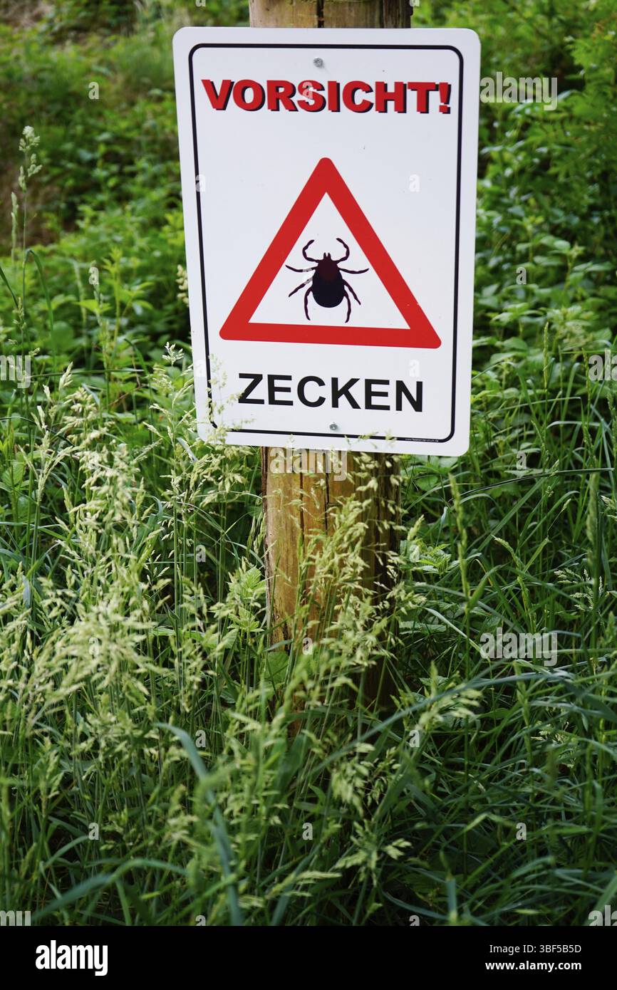 Warning sign against ticks in the middle of grass and green vegetation ...