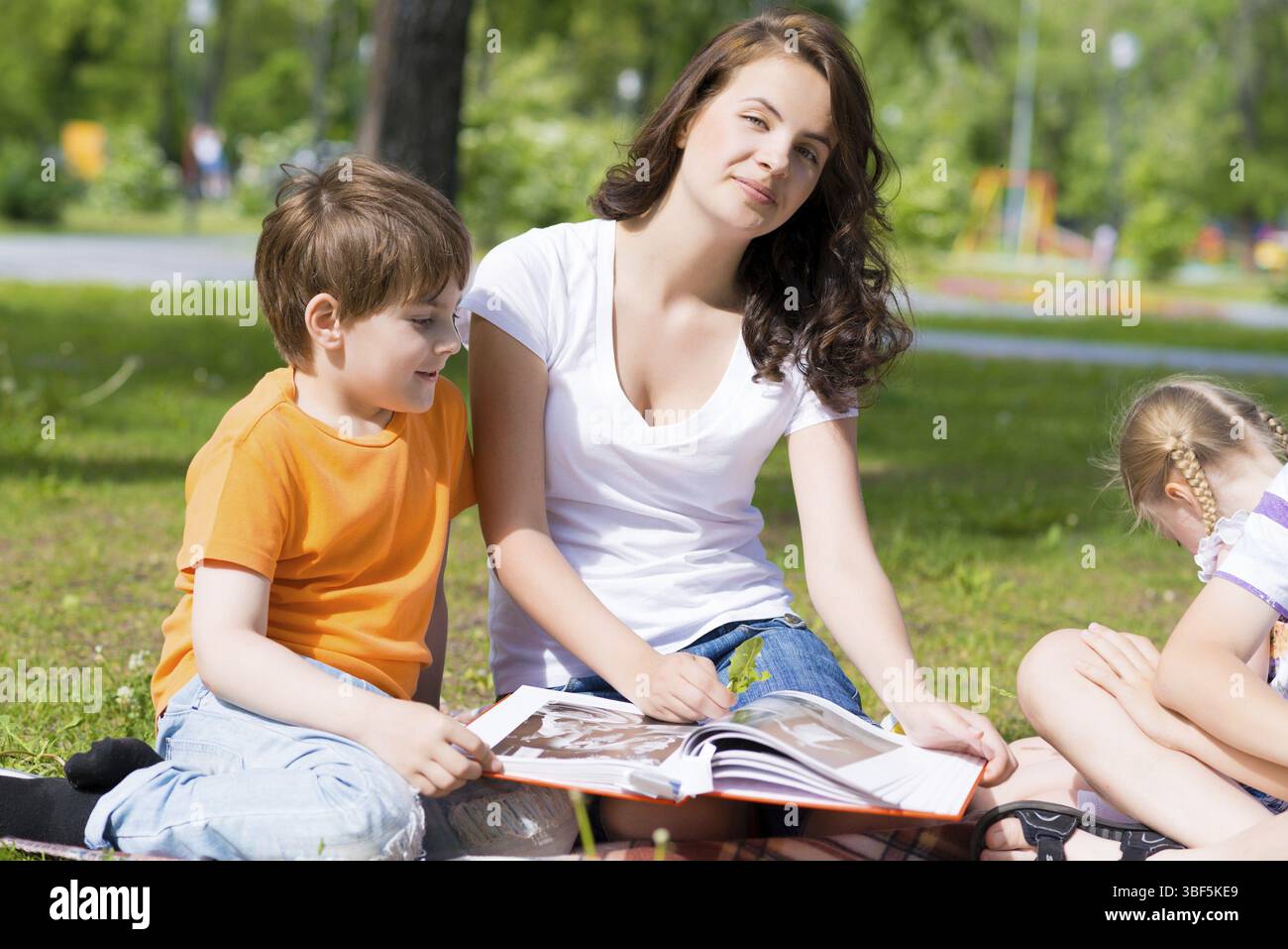 Children and teacher reading book together in the summer park Stock ...