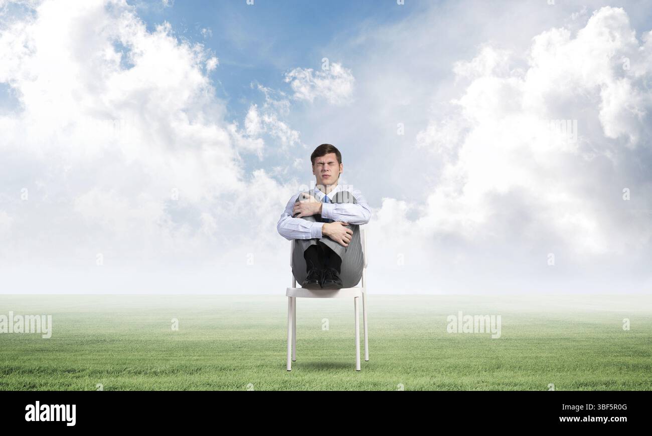 Scared businessman sitting on a chair with his hands clasped his knees ...