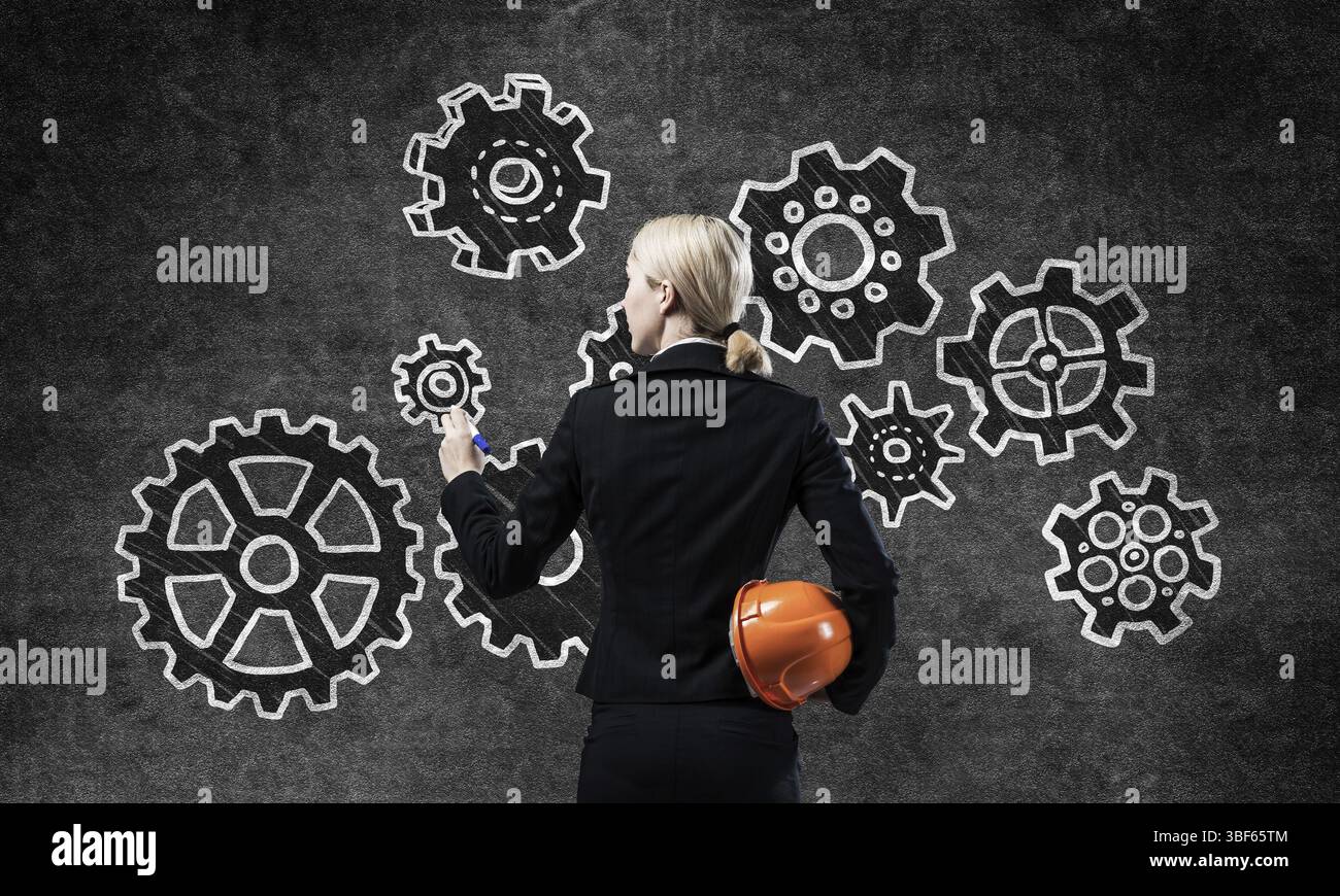 Businesswoman draws cogwheel mechanism on chalkboard. Woman in business ...