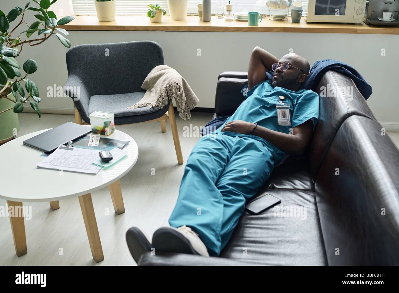 Medical professional reclining on couch in hospital room, wearing blue ...