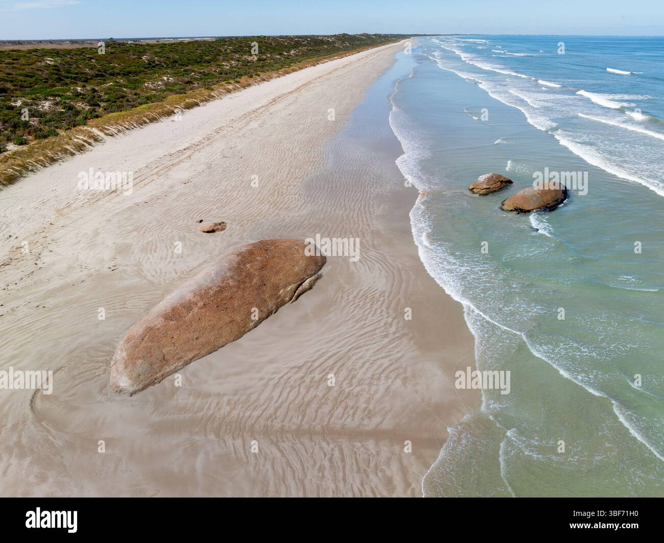 Aerial view of waves rolling around large granite bolders on a long ...