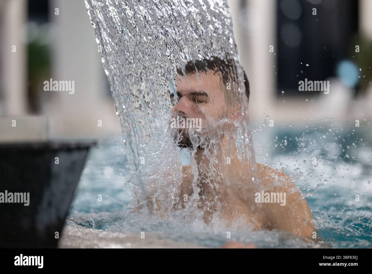 Man standing under a hydrotherapy waterfall in a spa pool, receiving ...