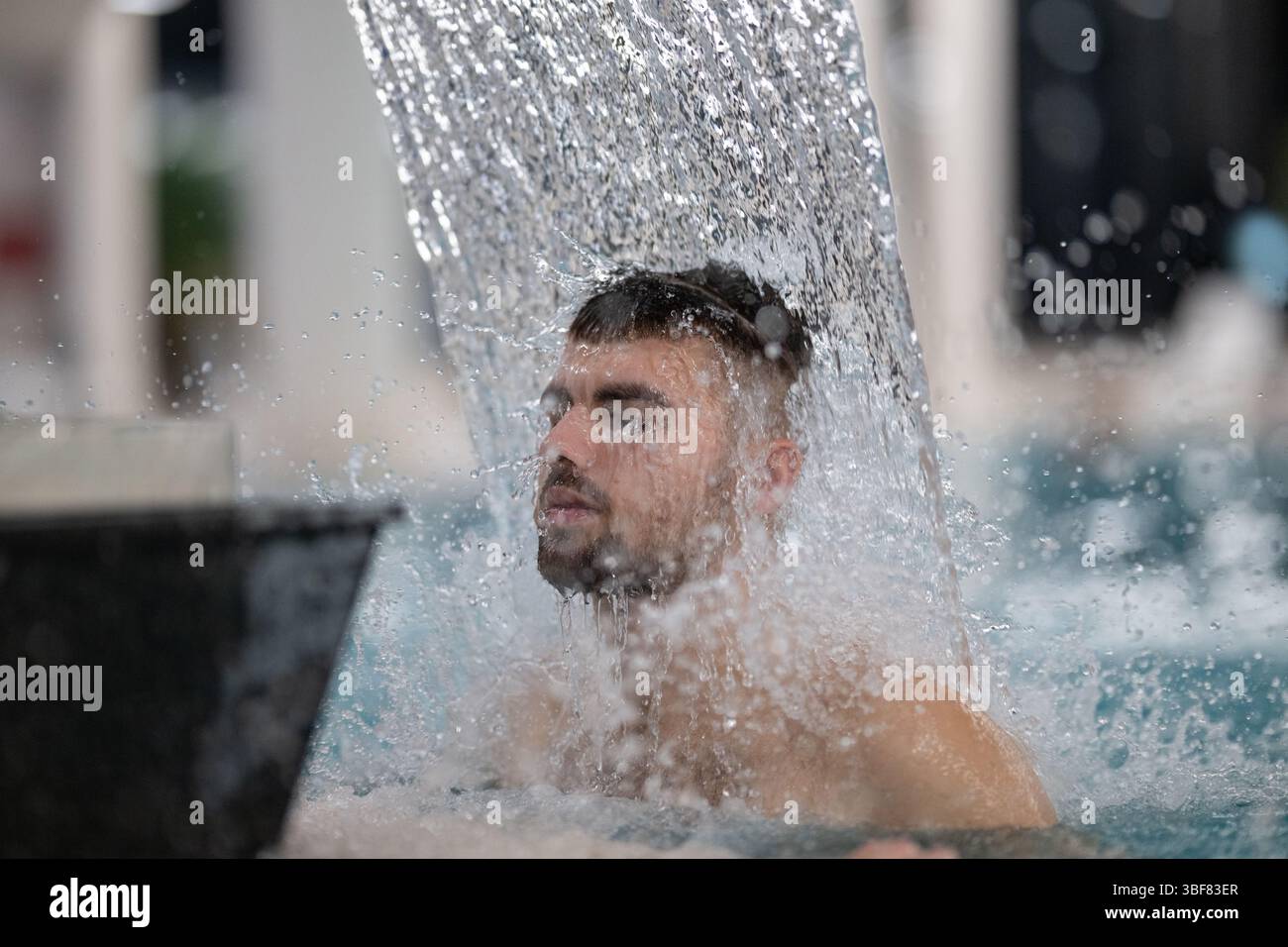 Man standing under a hydrotherapy waterfall in a spa pool, receiving ...