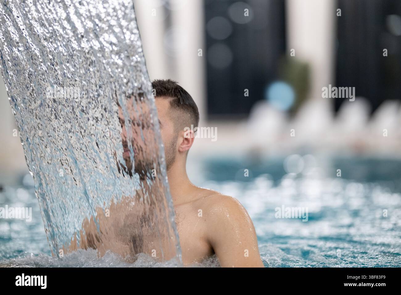 Man standing under a hydrotherapy waterfall in a spa pool, receiving ...
