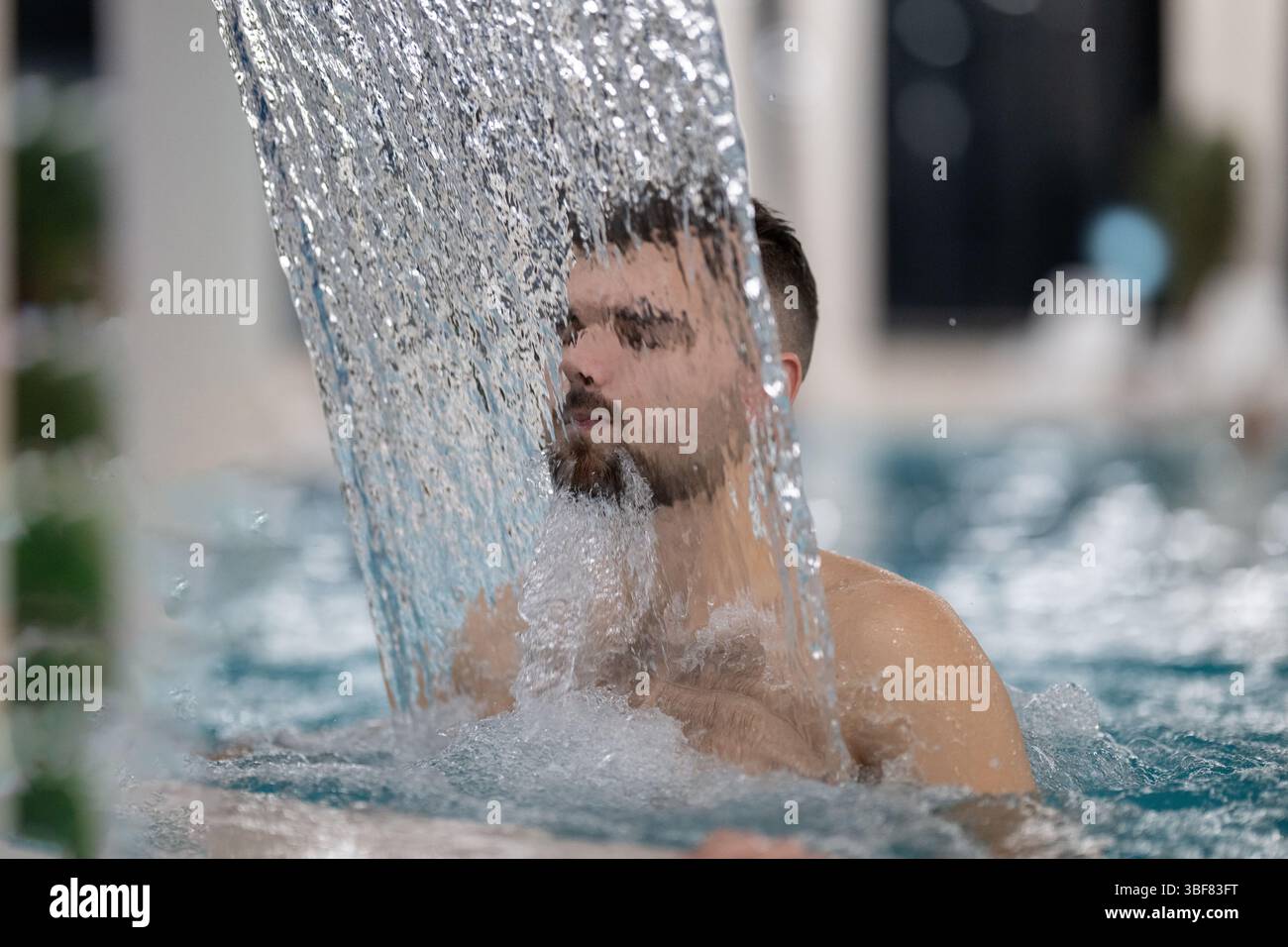 Man standing under a hydrotherapy waterfall in a spa pool, receiving ...