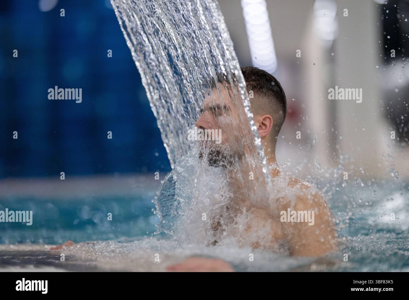 Man standing under a hydrotherapy waterfall in a spa pool, receiving ...