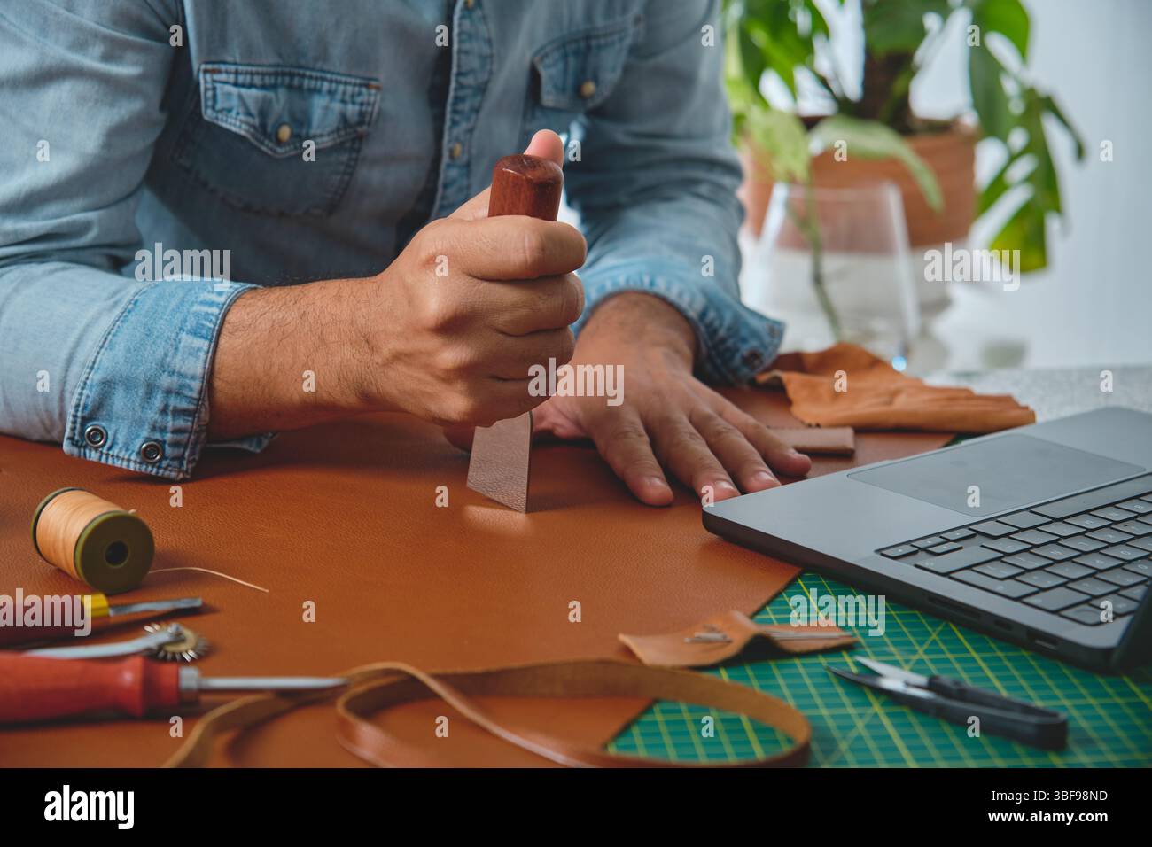 Leather craftsman working leather using tools and laptop in workshop ...