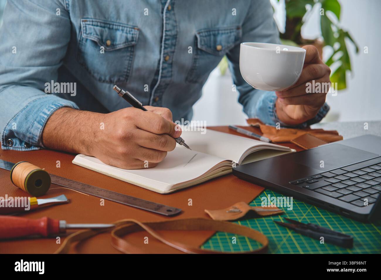 Leather craftsman drinking coffee and writing notes on notebook in his ...