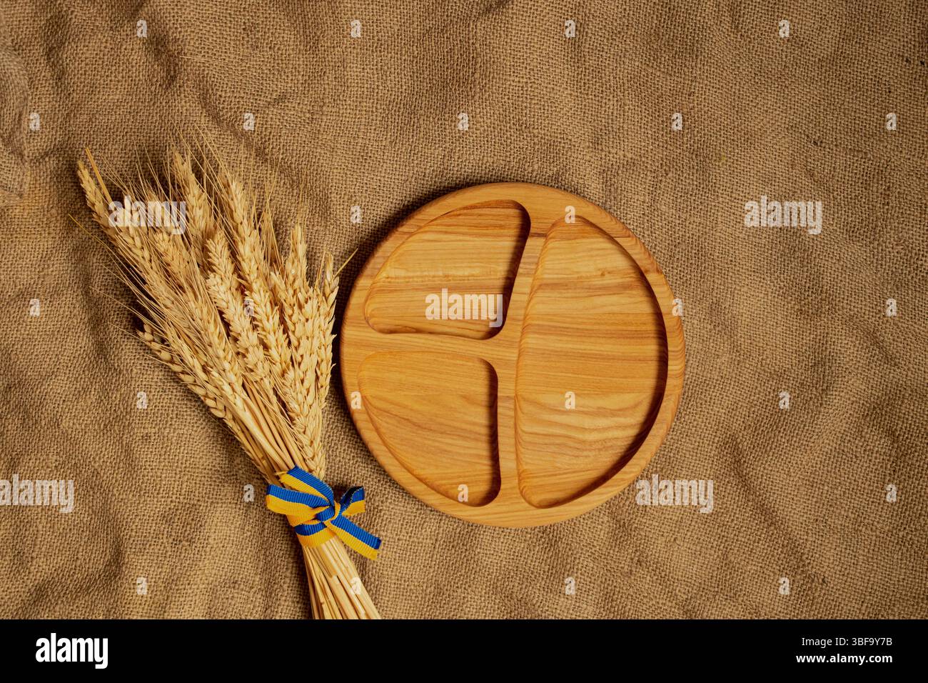 Wooden plate and wheat ears with Ukrainian flag ribbon on burlap ...