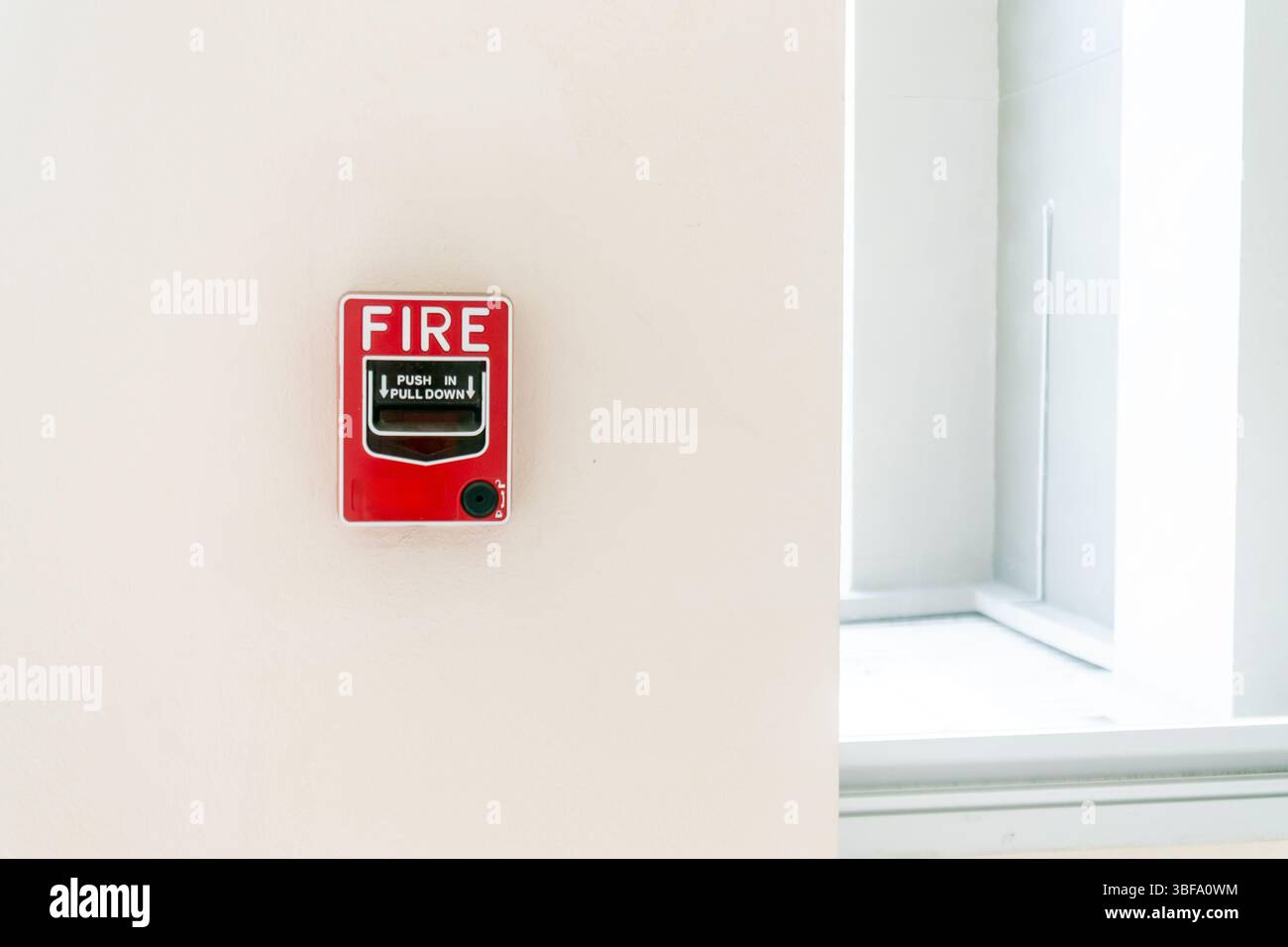 A vivid red fire alarm button mounted on a clean white wall portrays ...
