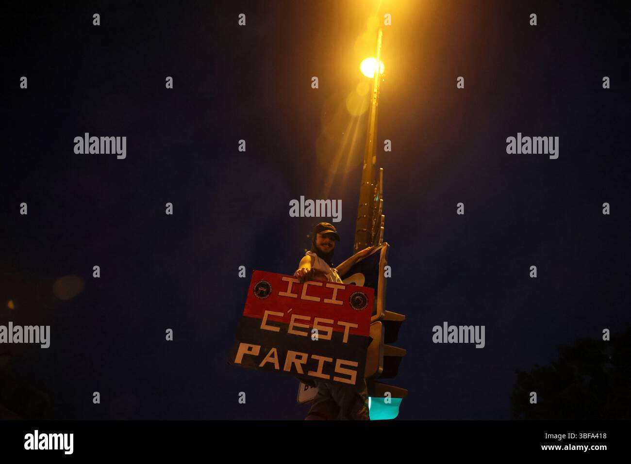A PSG supporter climbs a street lamp with a poster reading "Here it's ...