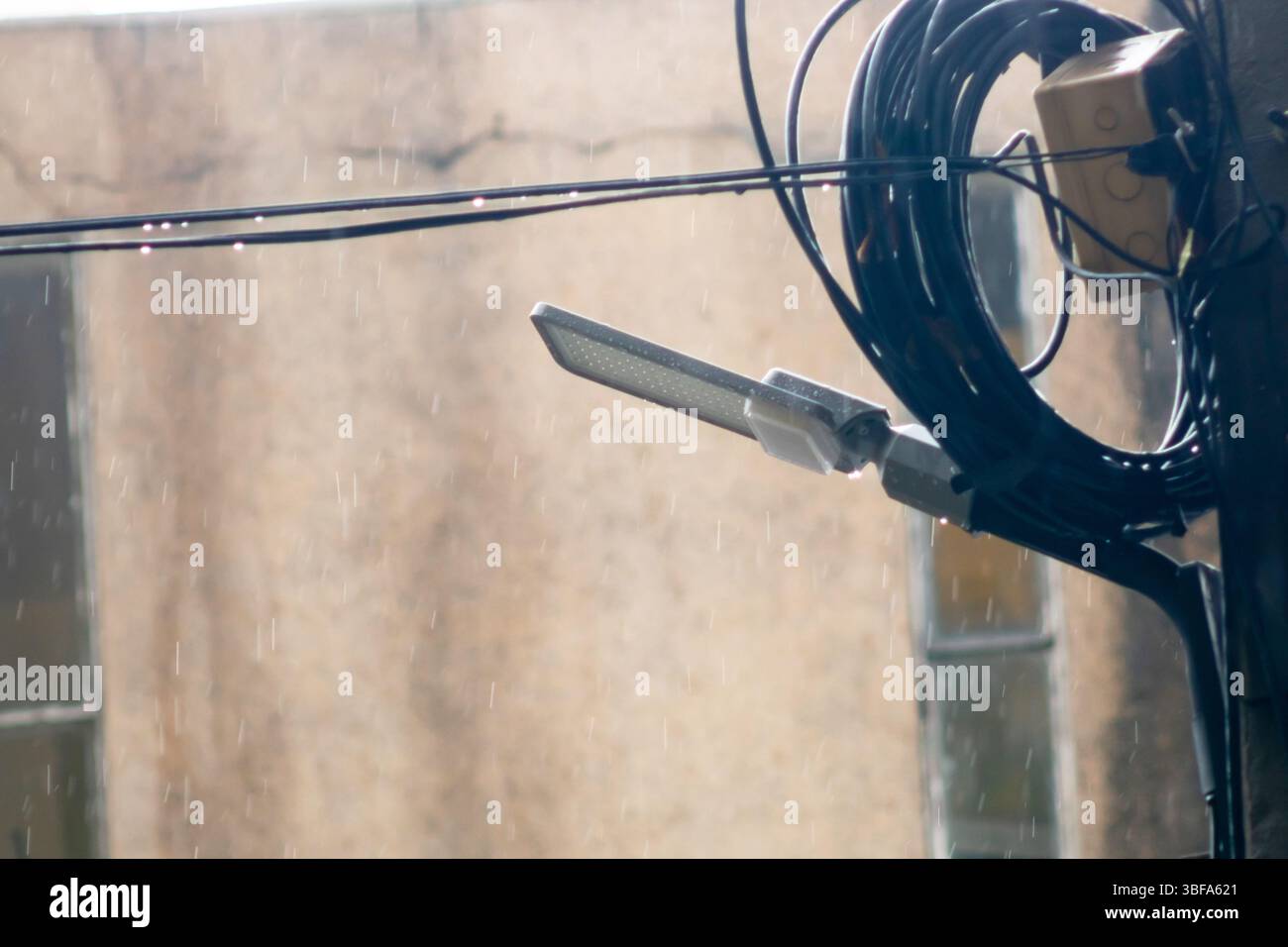 A close-up view of a street light amidst falling rain, with electrical ...