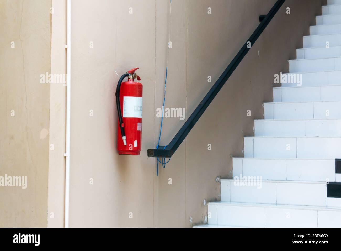 A bright red fire extinguisher mounted on a wall beside a staircase ...