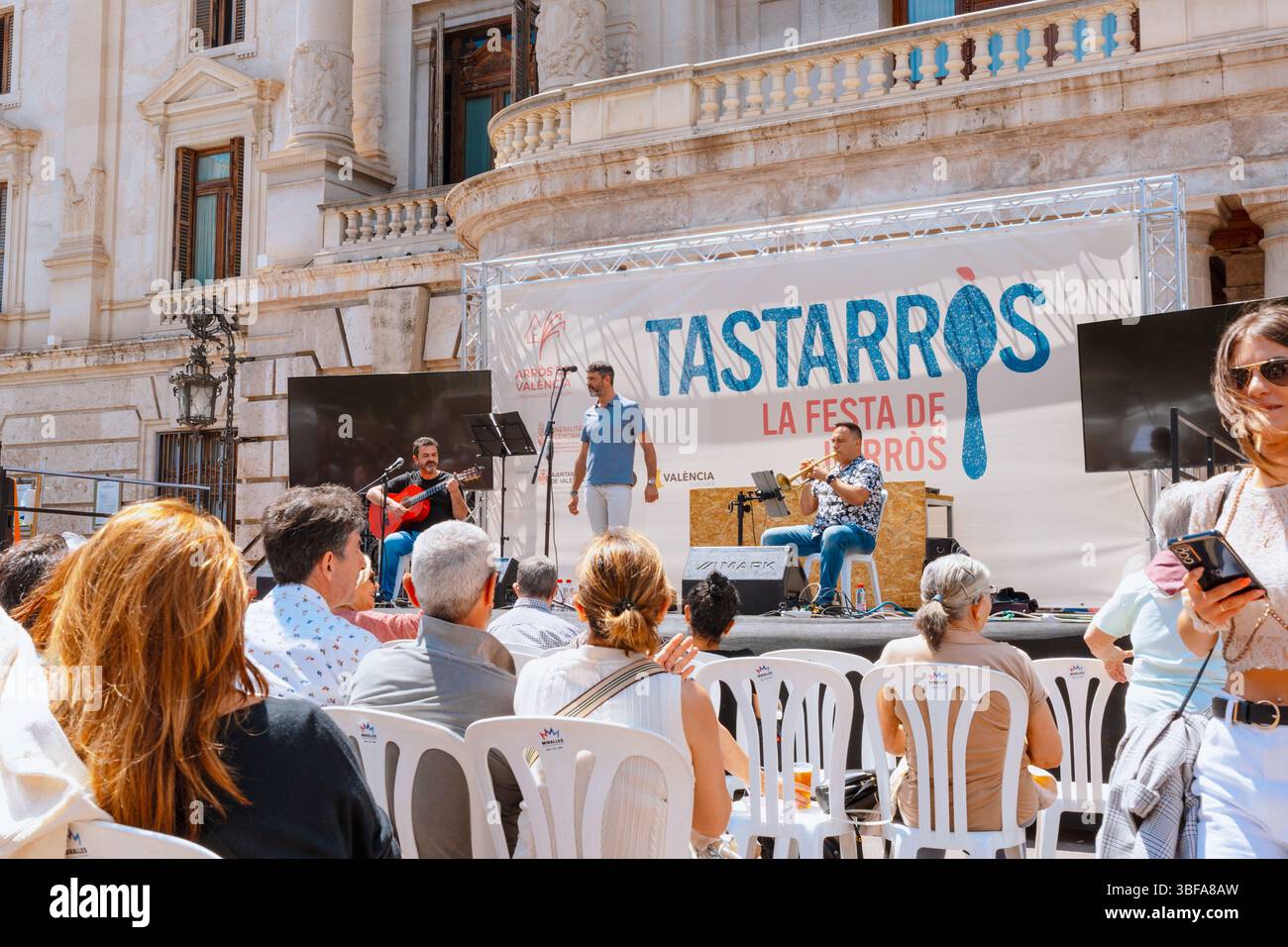 Seated audience watches singer, guitarist, and trumpet player onstage ...