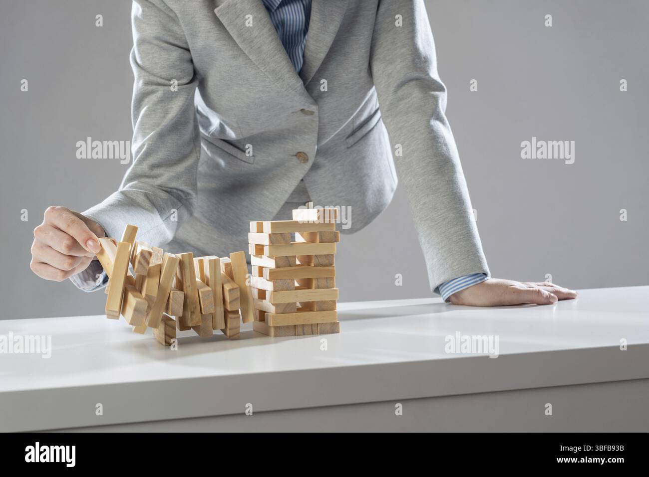 Businesswoman removing wooden block from falling tower on table ...