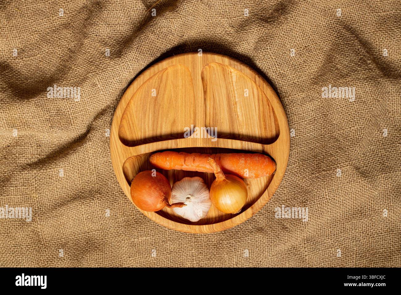 Wooden plate with onion, garlic and carrot on burlap, natural ...