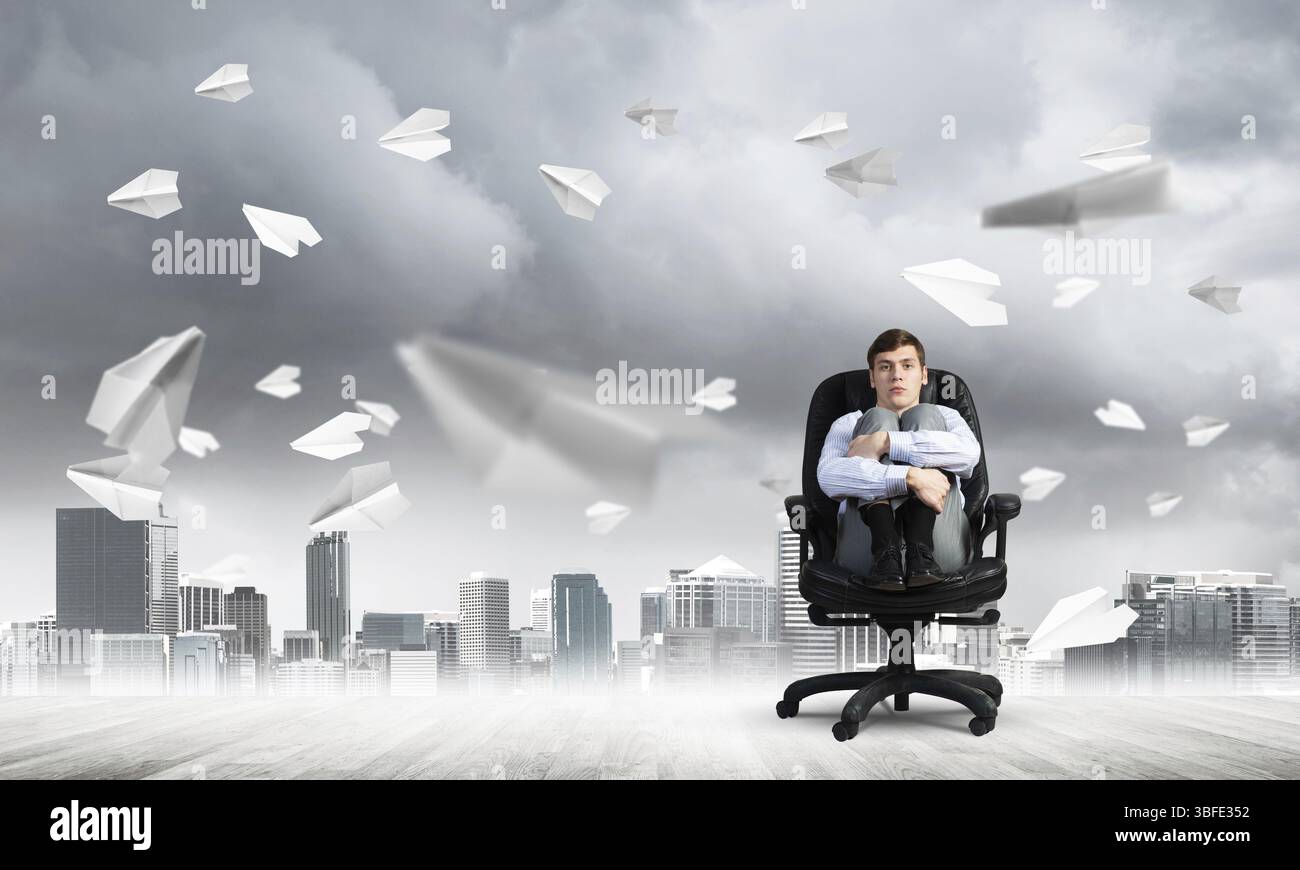 Scared businessman sitting on a chair with his hands clasped his knees ...