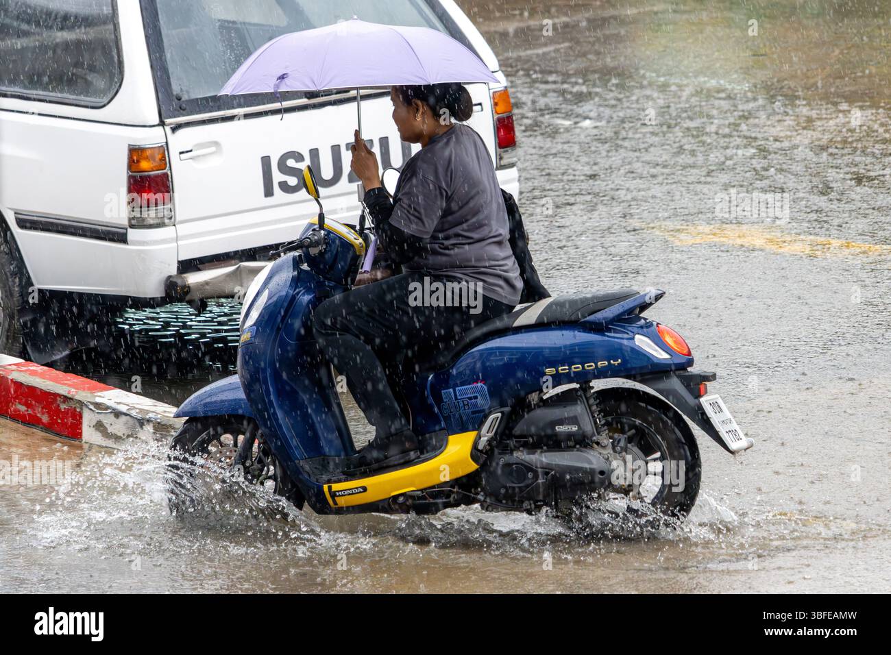 SAMUT PRAKAN, THAILAND, MAY 16 2025, Woman on motorbike rides through puddle in rain while ...
