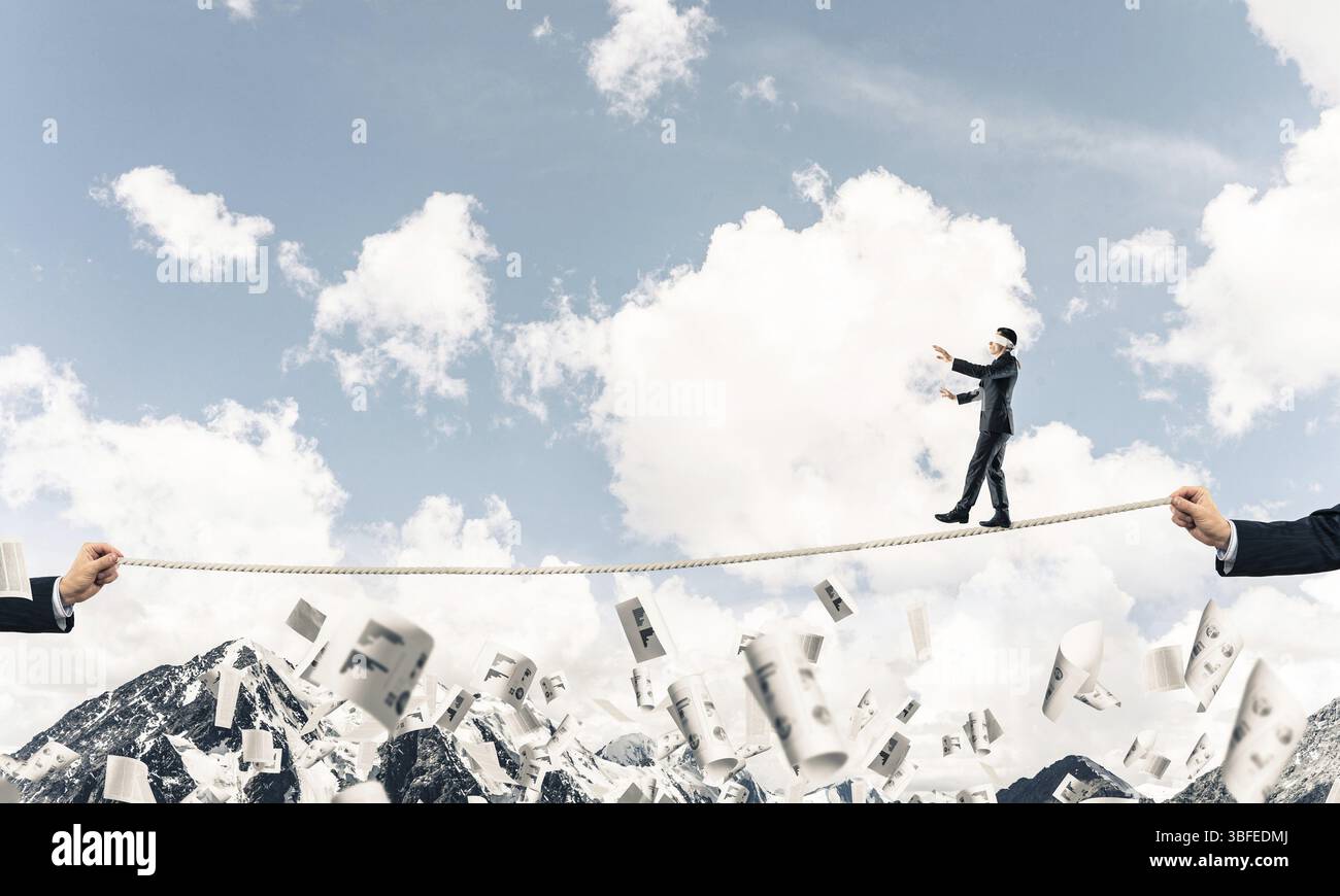 Businessman walking blindfolded on rope among flying documents and ...