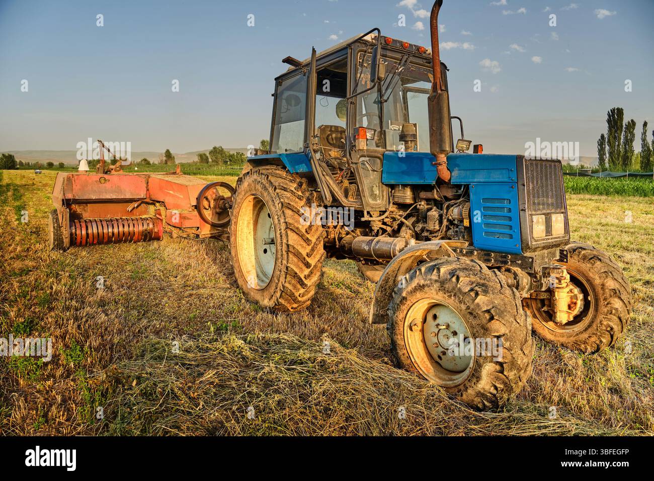 Vintage hay baler attached to a tractor on a sunlit field during ...