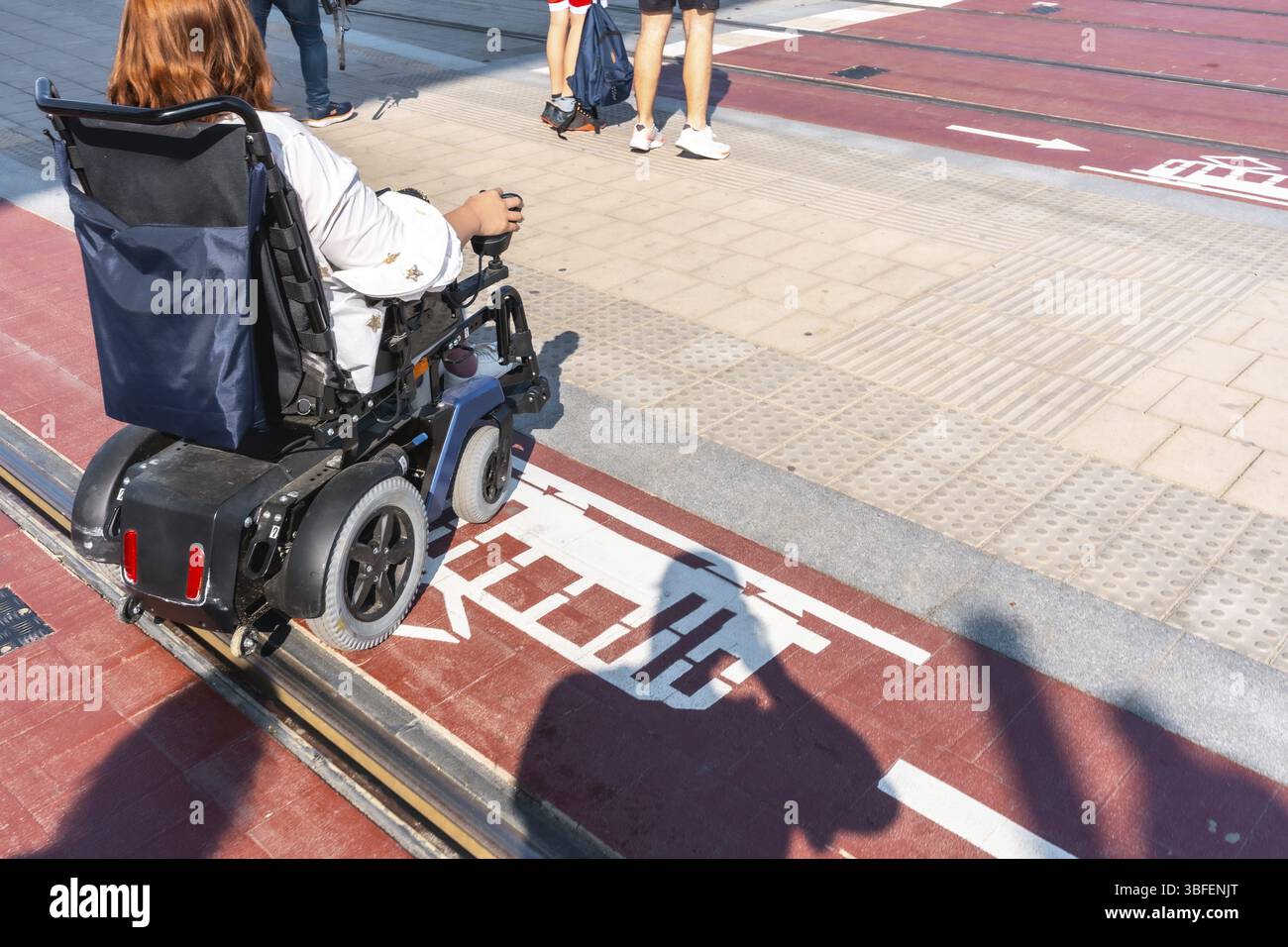 Woman navigating an electric wheelchair across designated tram tracks ...