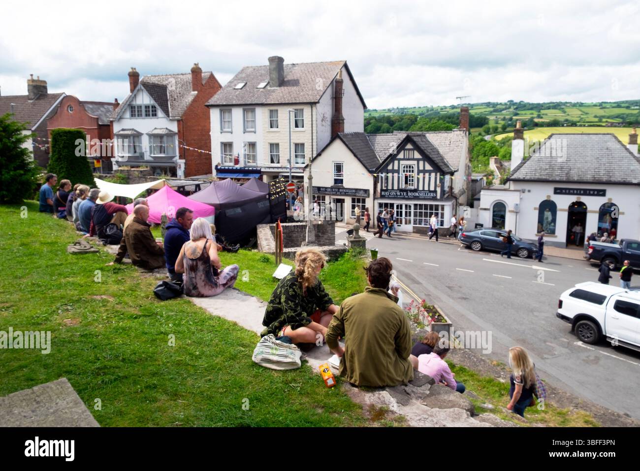 People visitors sitting on stone wall in town centre by Hay Castle ...