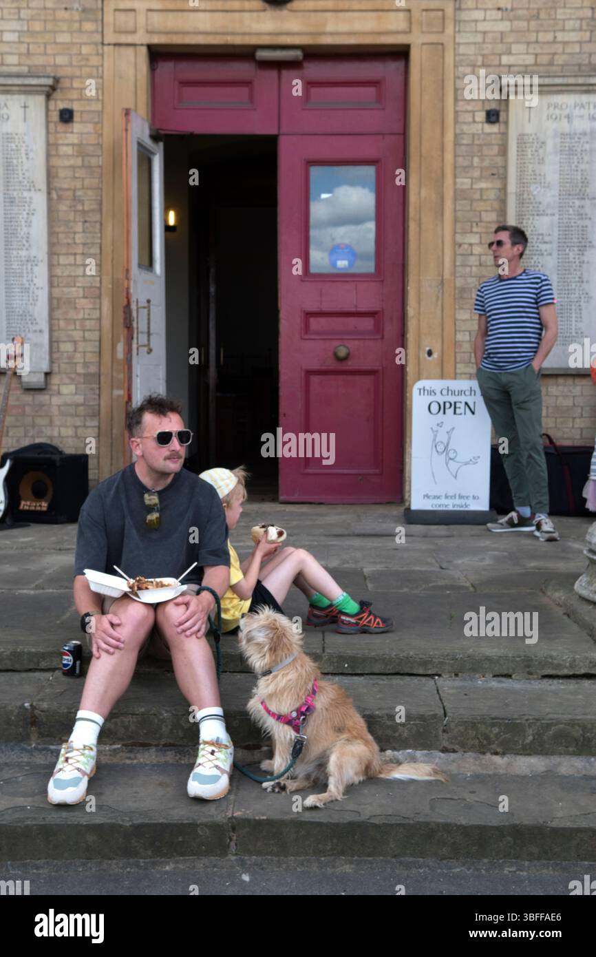 Church Open sign UK. Father, son and dog sitting on church steps eating ...
