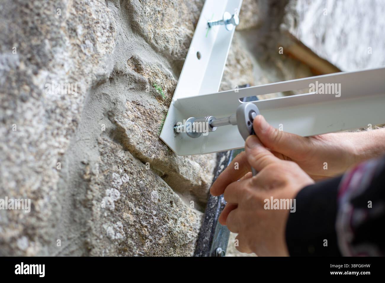 A man uses a ratchet wrench with a socket to screw a screw into a metal ...