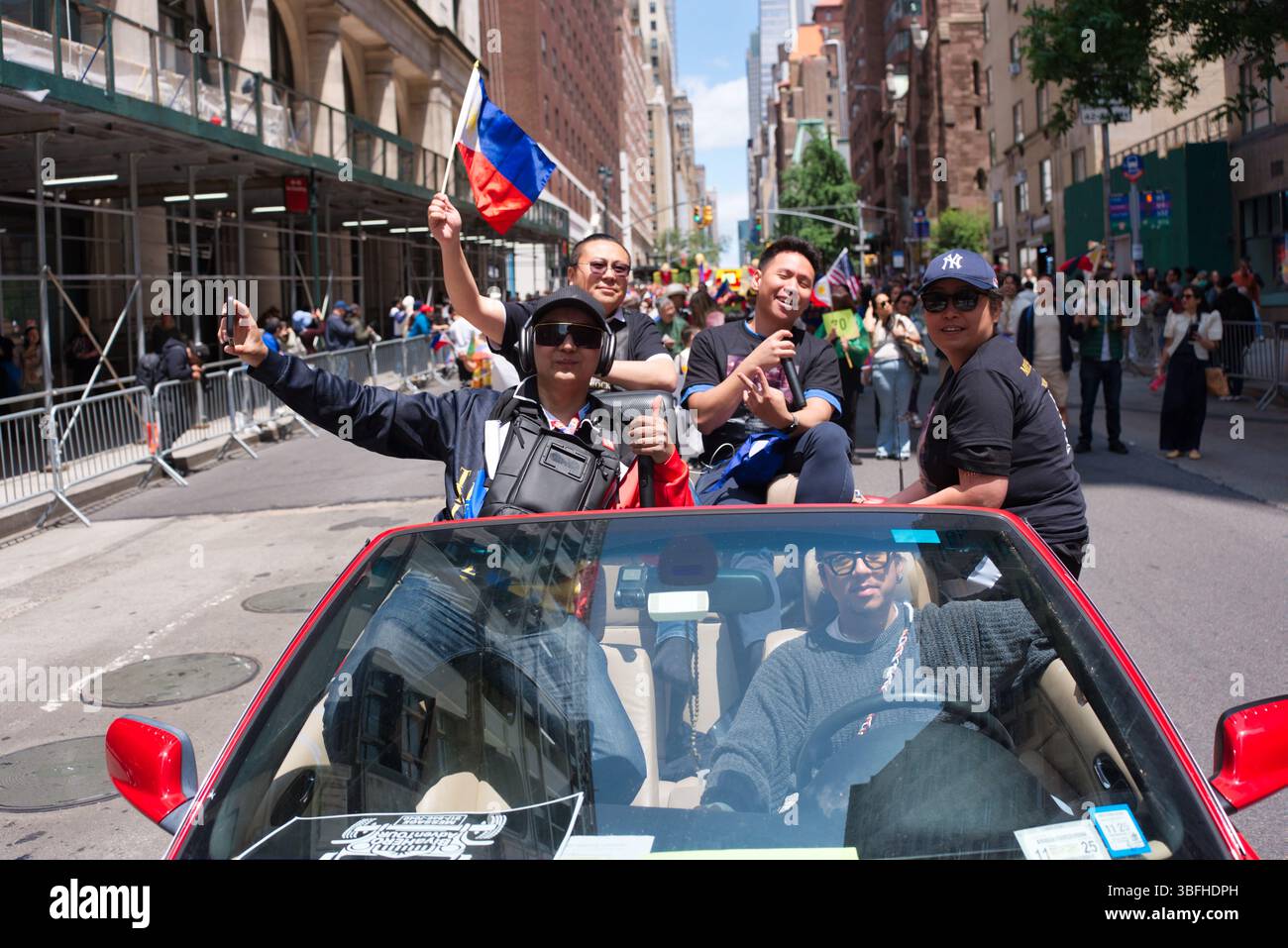 Five Filipino people ride in a red convertible during a parade, waving ...